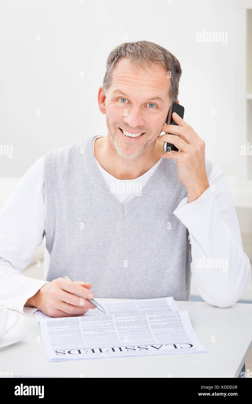 Man Talking On Cellphone While Reading Classifieds On Newspaper Stock ...