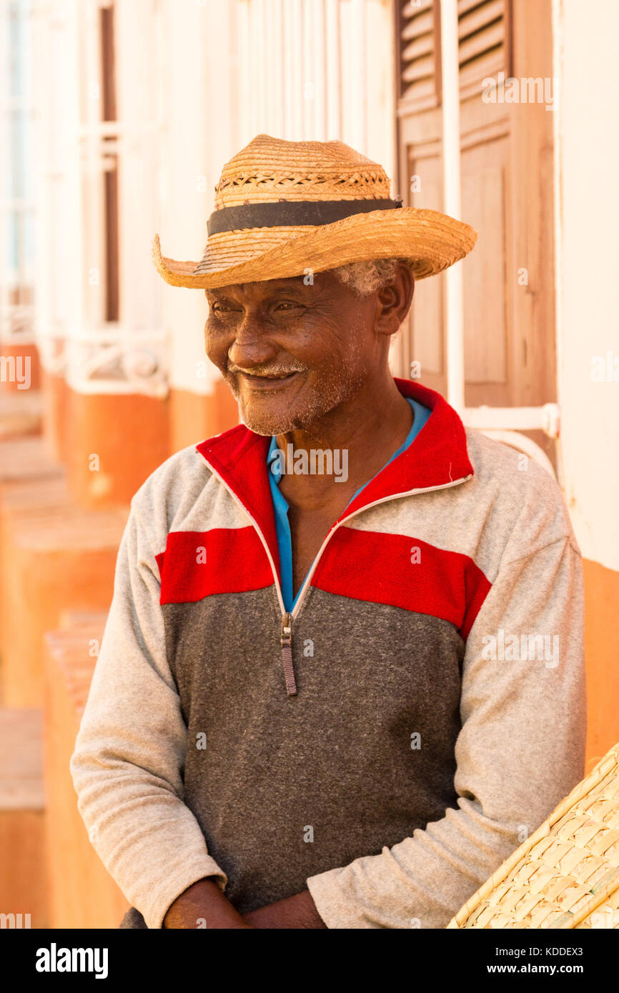 Smiling local Cuban man with hat sitting outside a house watching the ...