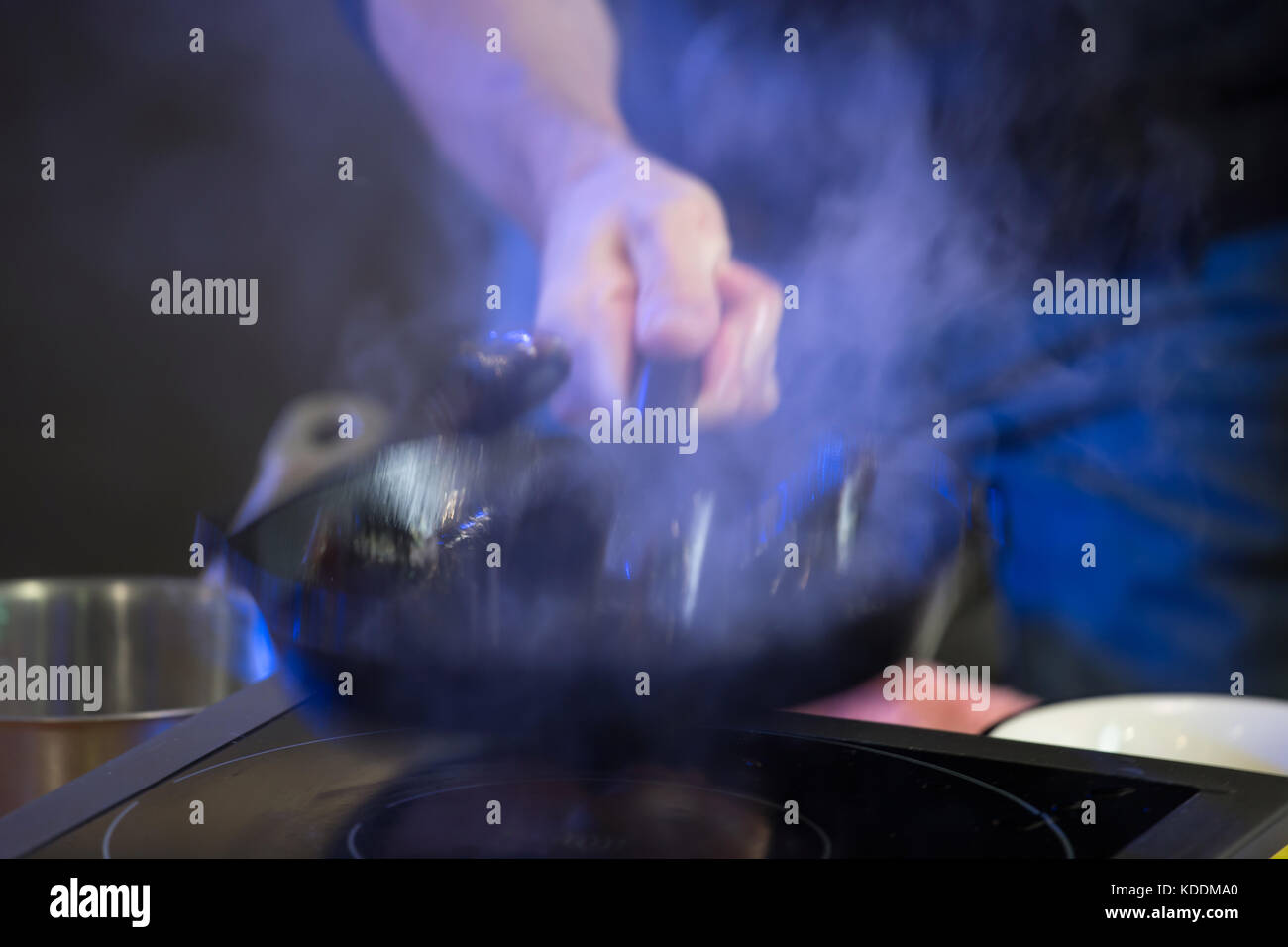 Cook's hand holds a steaming frying pan over the stove. Shooting with ...