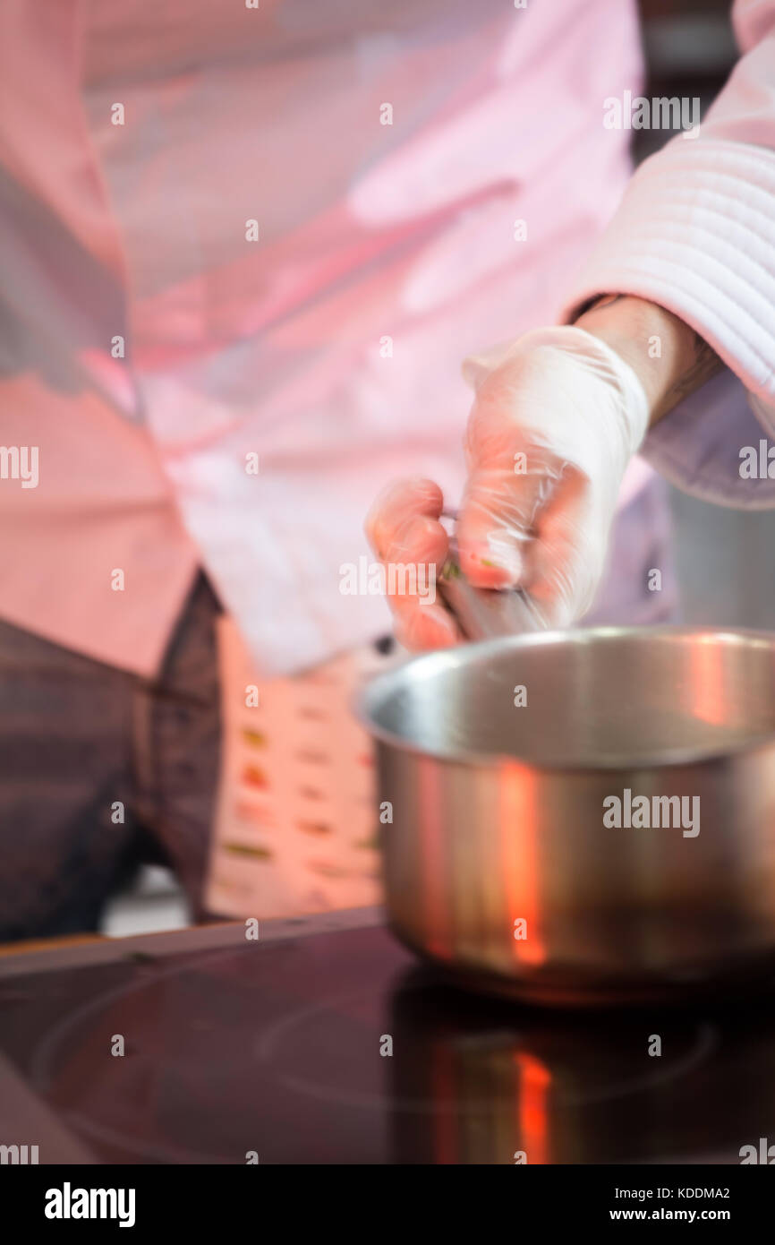 Cook's hand in white gloves and robe keeps the pan over the electric ...