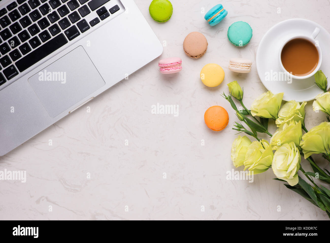 White desk with colorful macaroons, flowers, notebook, laptop and cup ...