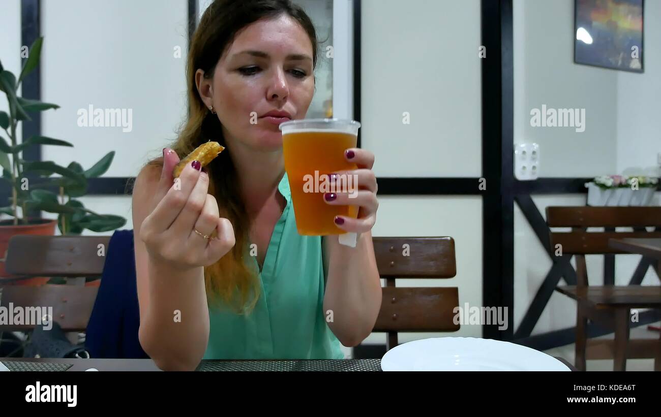 The girl is drinking beer in the bar. Woman drinks beer and eats fish ...