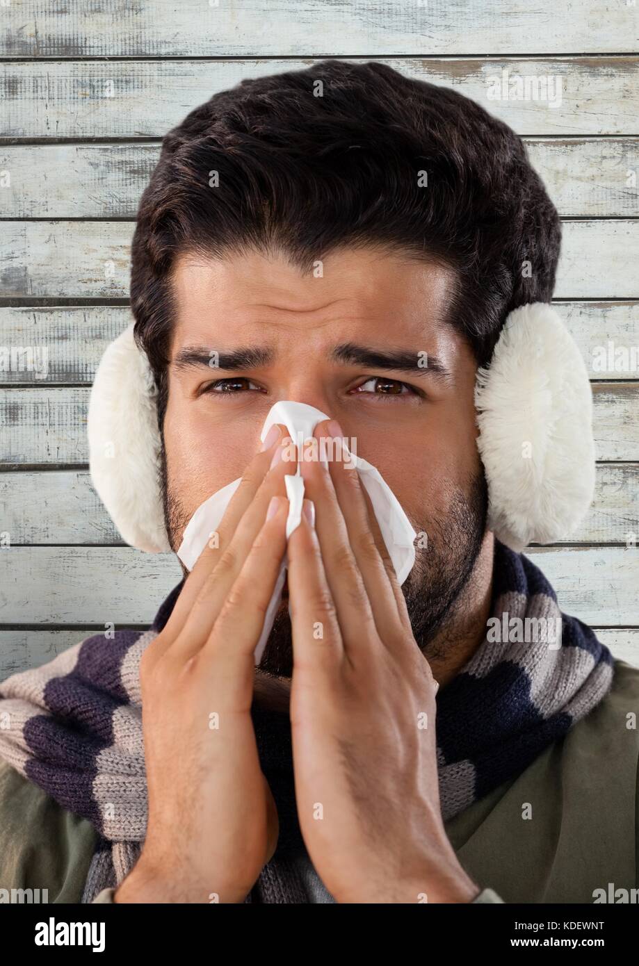 Digital composite of Man against wood with ear muffs and blowing nose ...