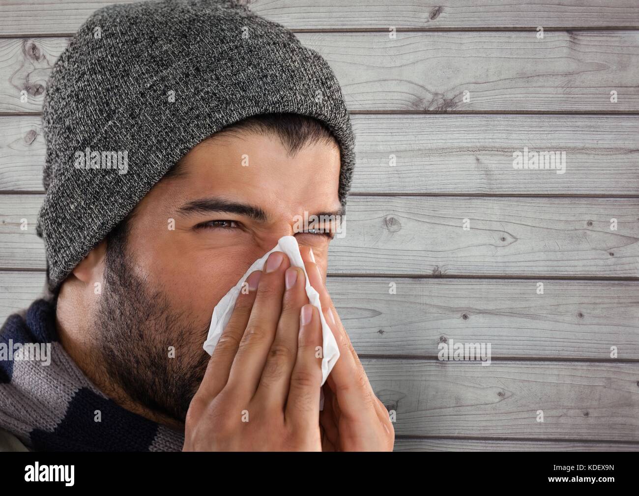 Digital composite of Man against wood with warm hat blowing nose in ...