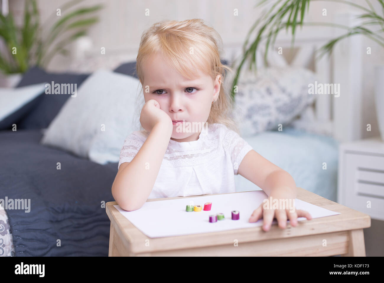 Sulky grumpy attractive little blond girl sitting with paper and ...