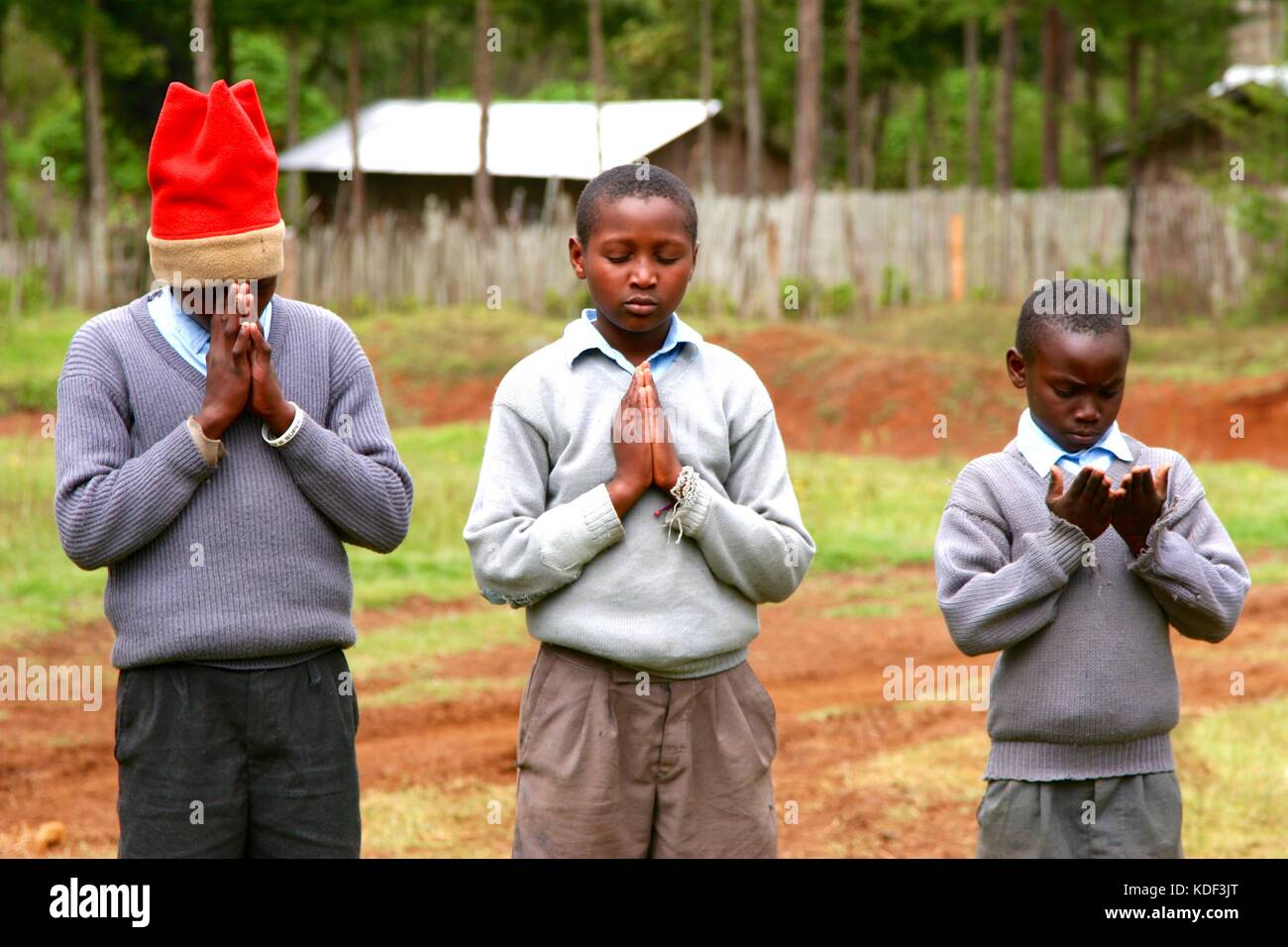 Three african school boys in a line praying before class, one of them ...