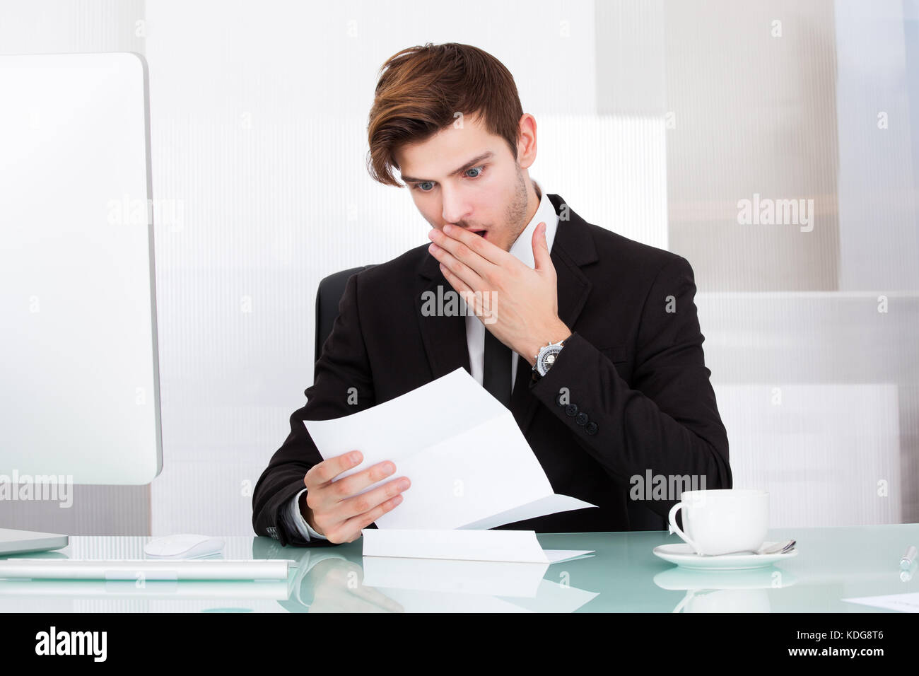 Shocked Businessman With Hand On Mouth Looking At Paper Stock Photo - Alamy