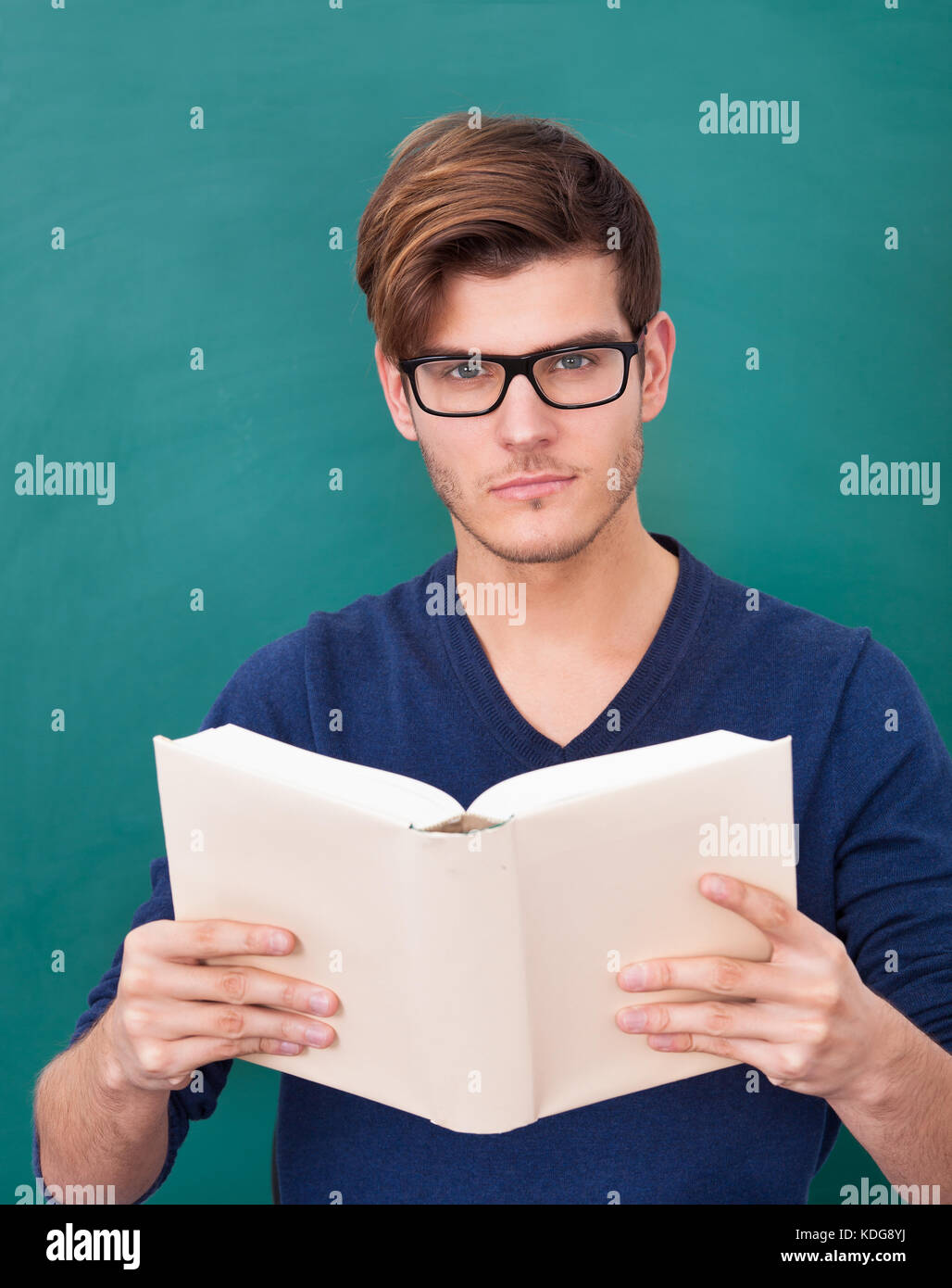 Portrait Of A Young Student Holding Book In Front Of Green Chalkboard ...