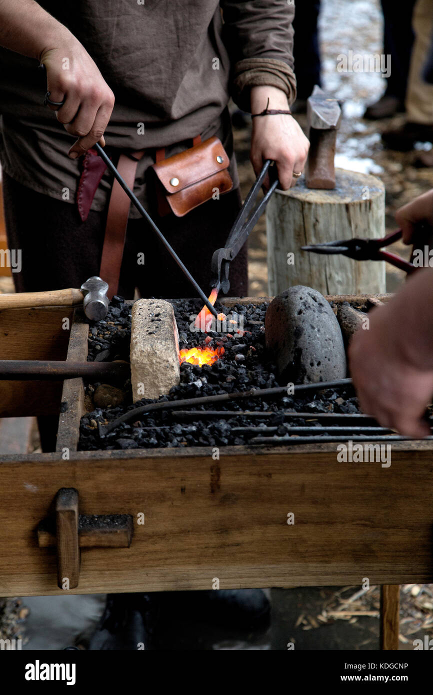 Blacksmith heating a piece of iron in his smithy. Iron is glowing hot ...
