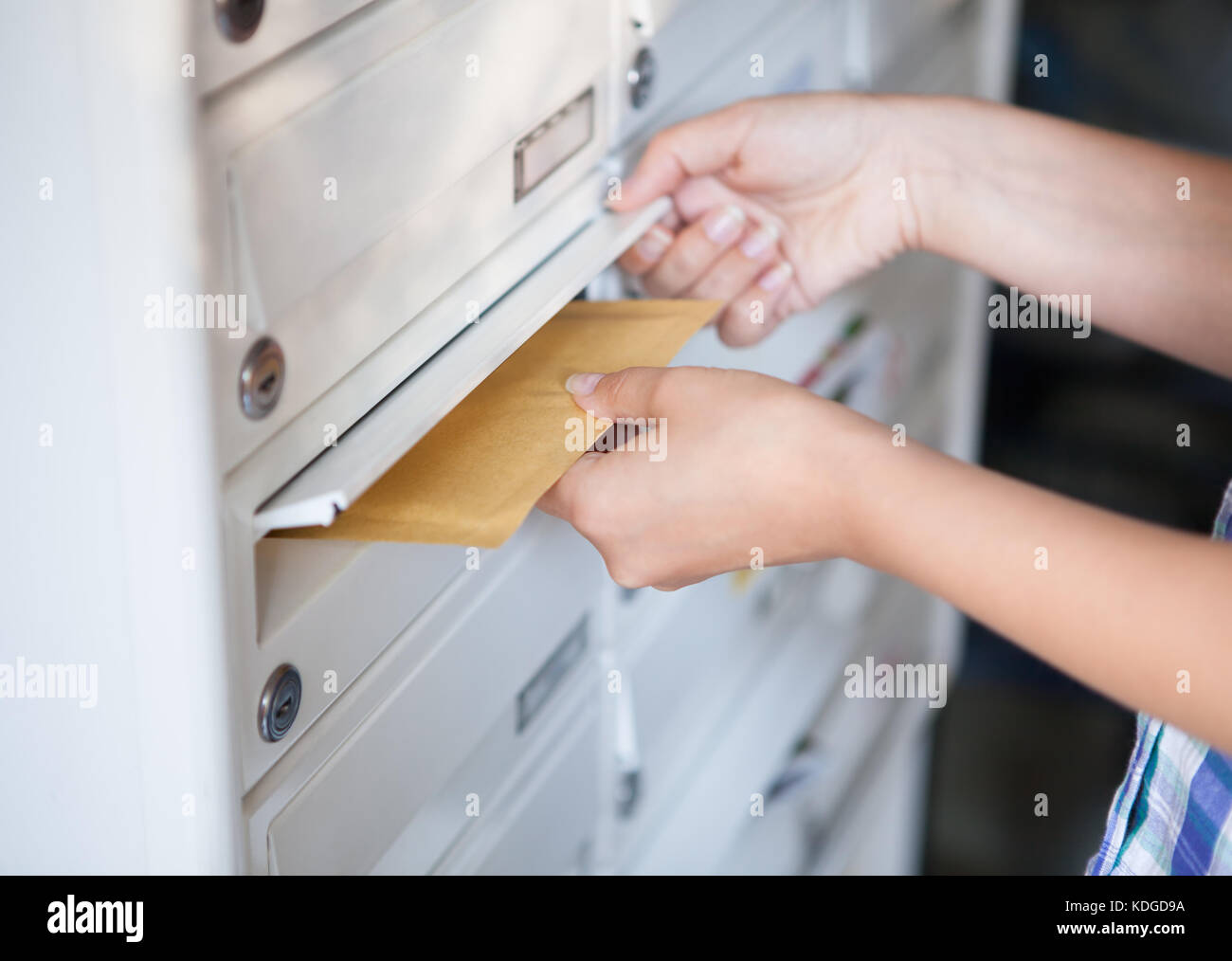 Close-up of woman's hand holding envelope and inserting in mailbox ...