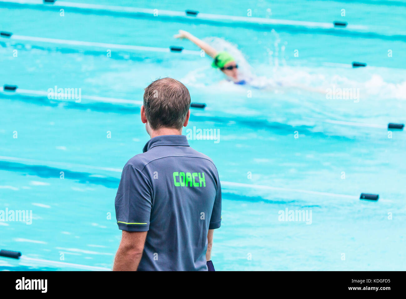 male swimming coach standing by the swimming pool in the rain watching ...