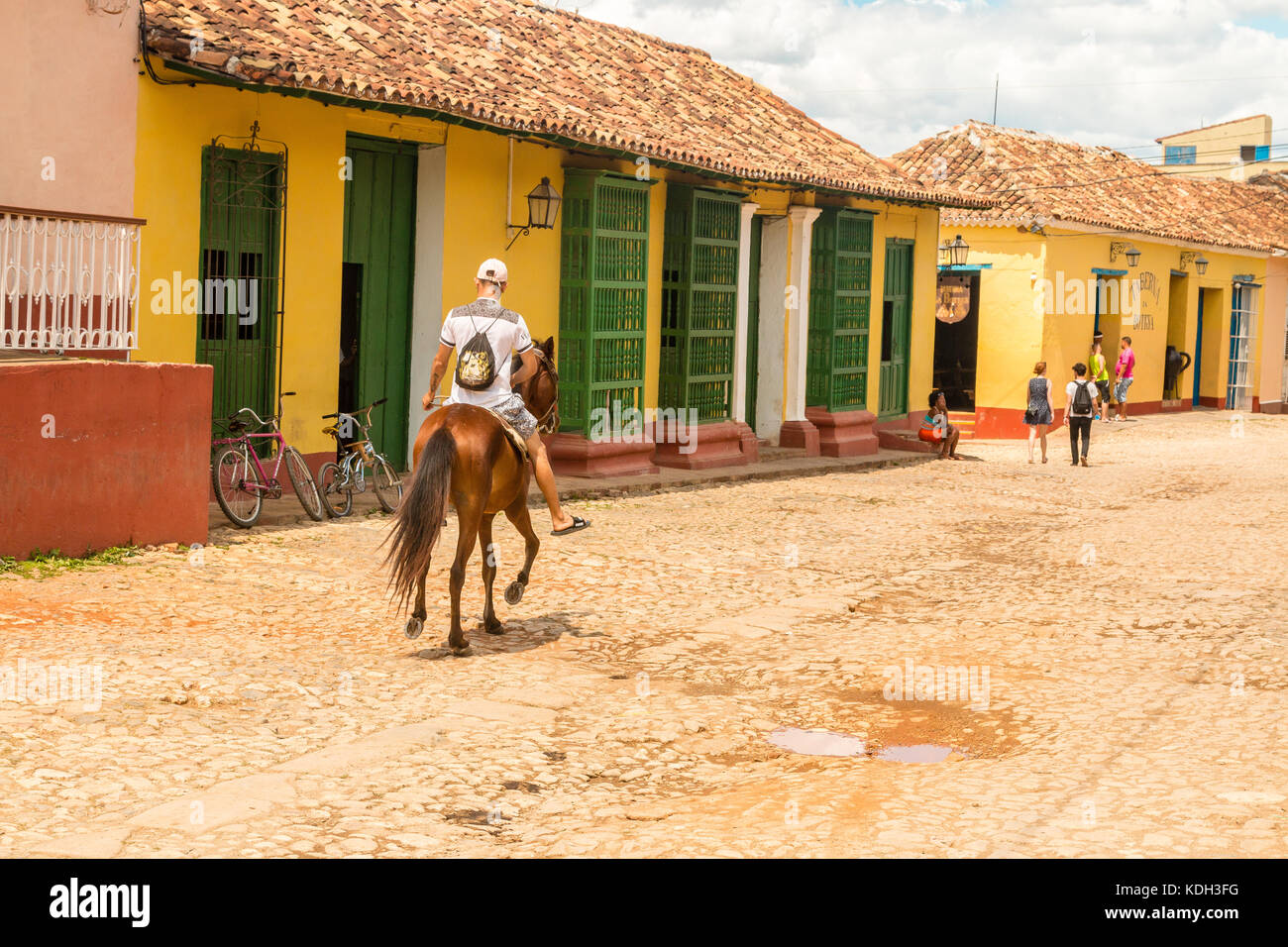 Cuban cowboy rides horse past th brigtly coloured l houses on the ...