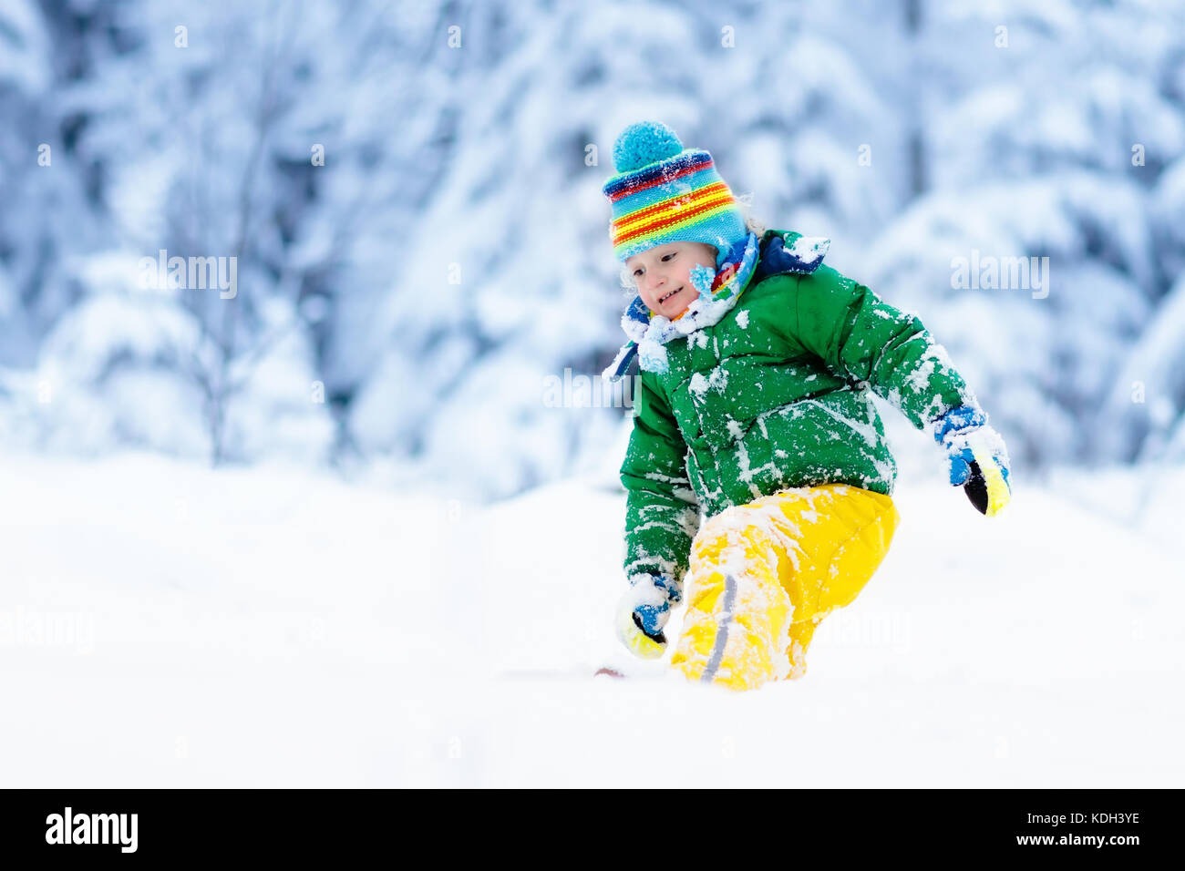 Child playing with snow in winter. Little boy in colorful jacket and ...