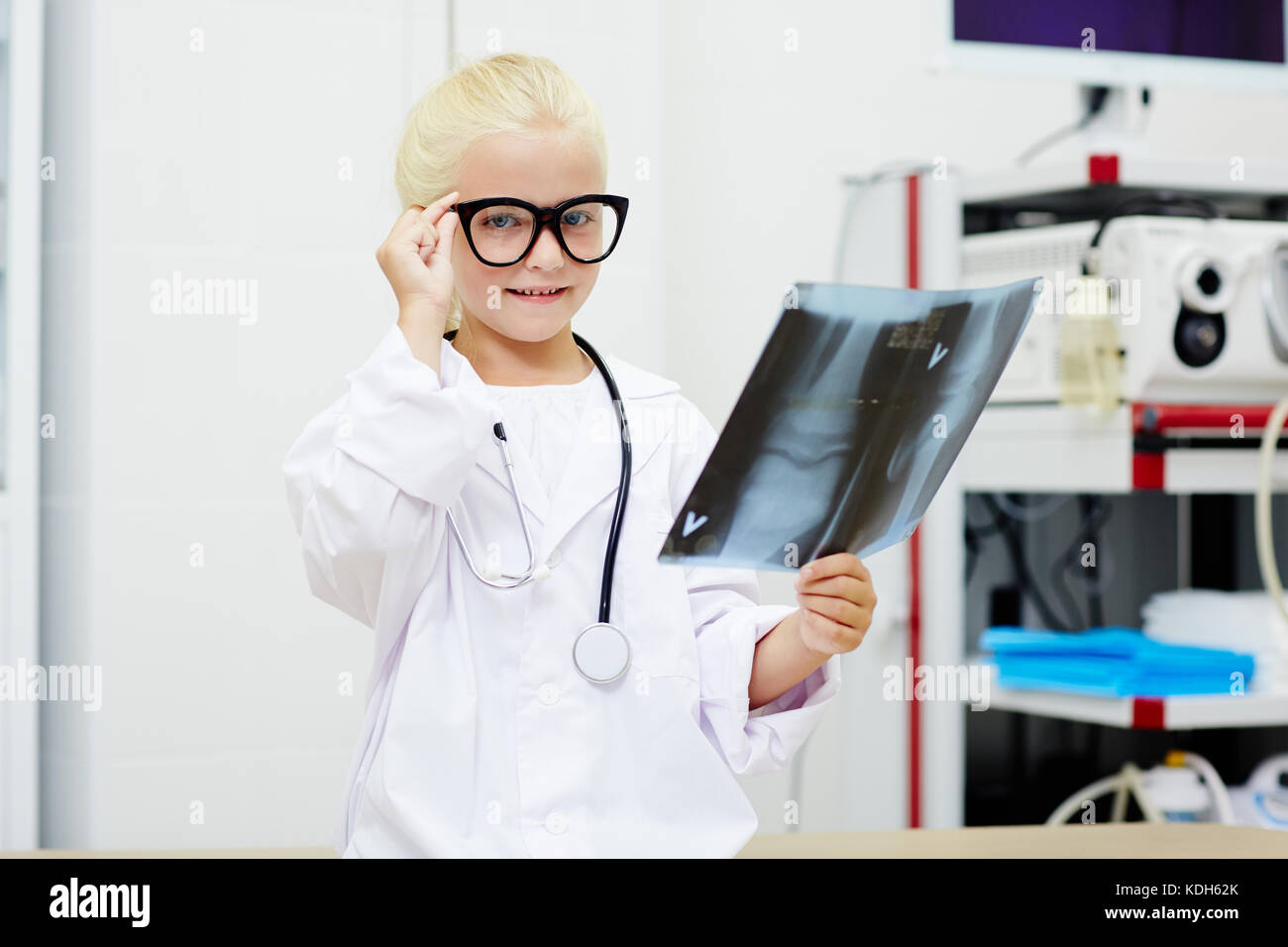 Cute little radiologist with x-ray result looking at camera in hospital ...