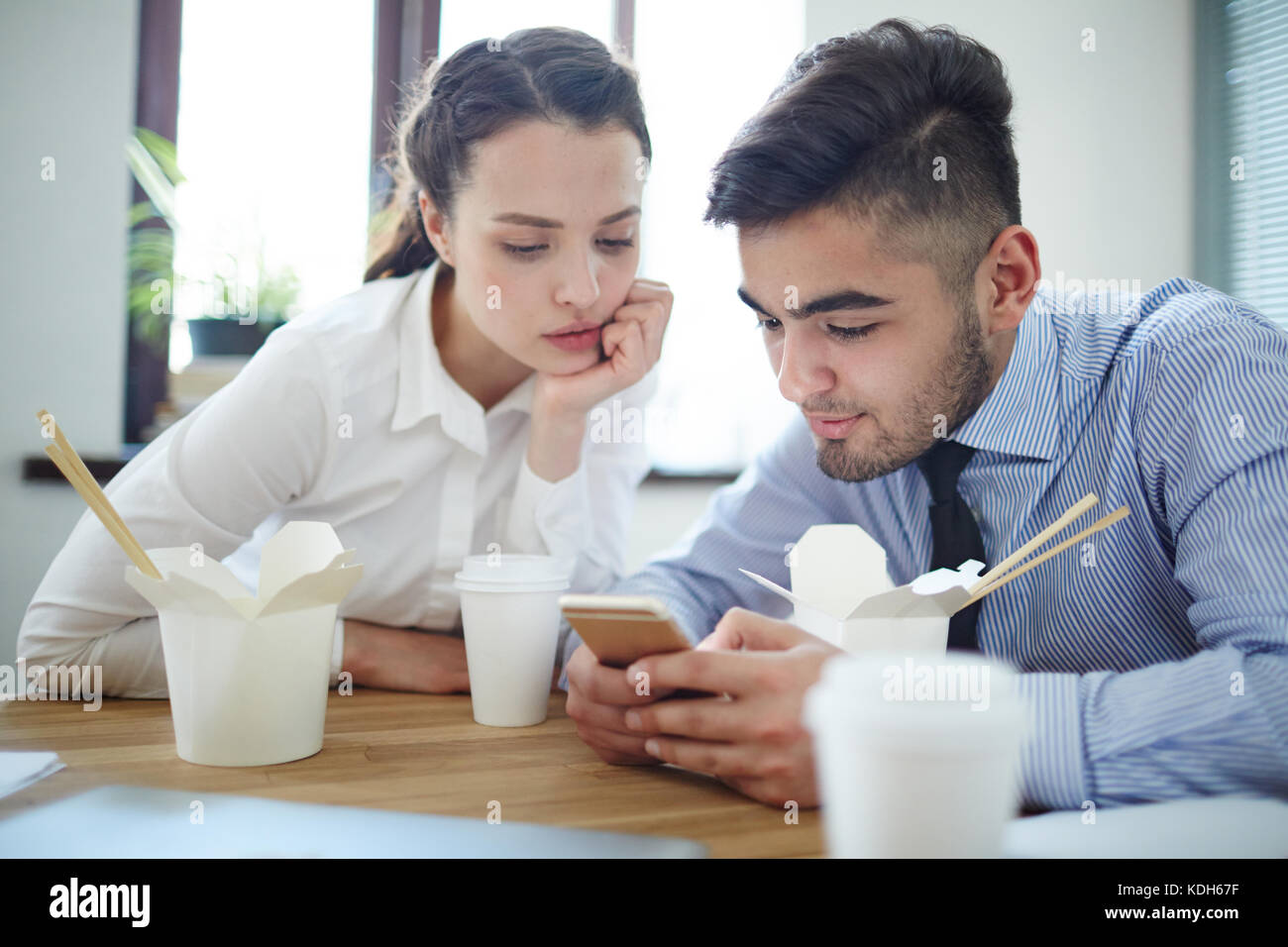 Attentive co-workers waching curious things in smartphone net at lunch ...