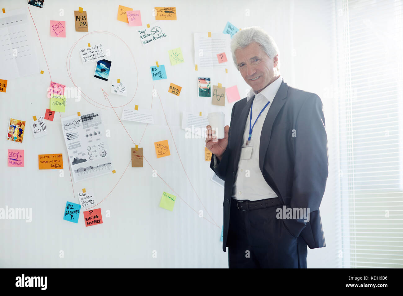 Elegant detective in suit standing by whiteboard with evidence of ...