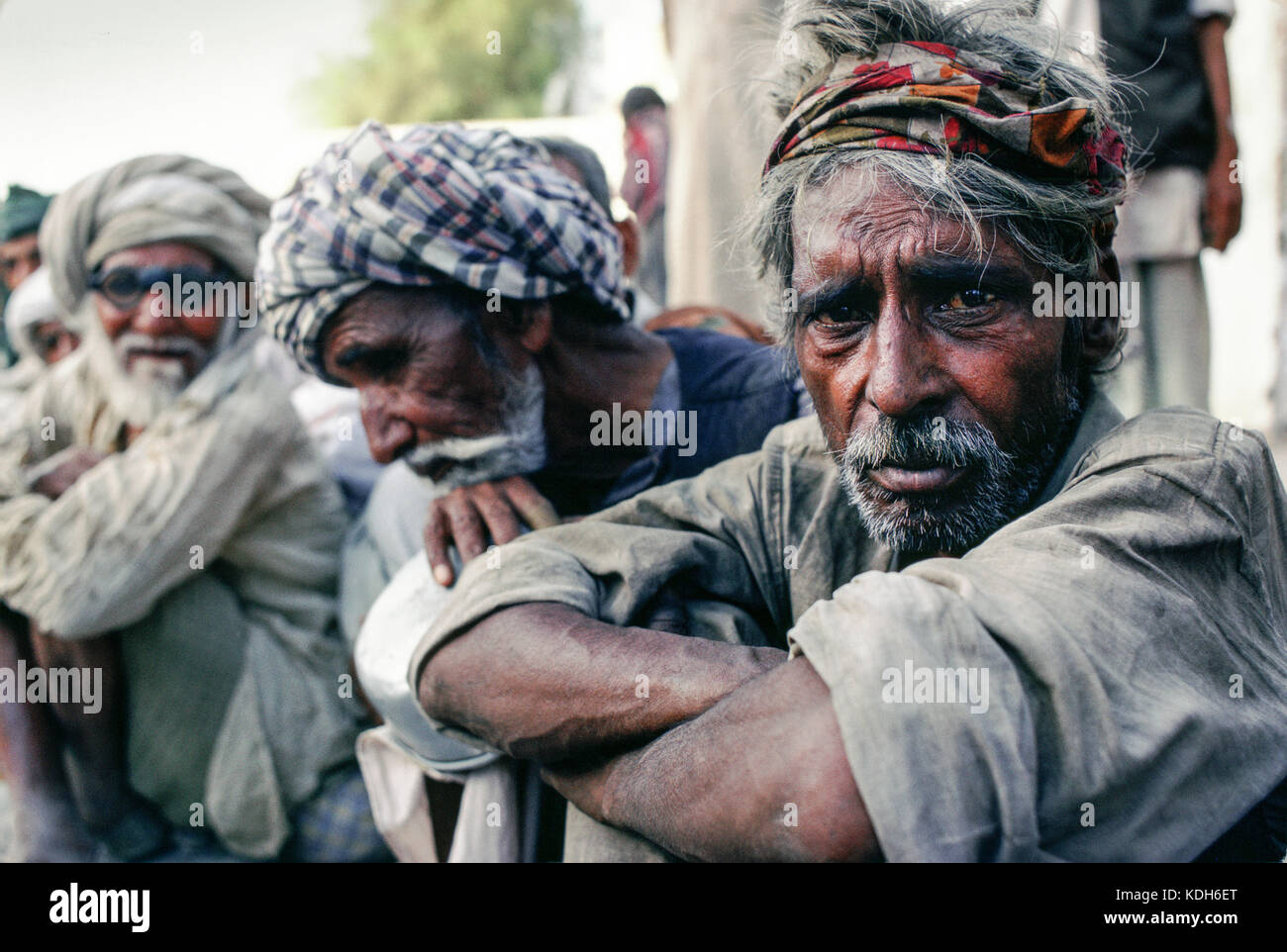 A group of railway porters sit together outdoors, wearing turbans and ...