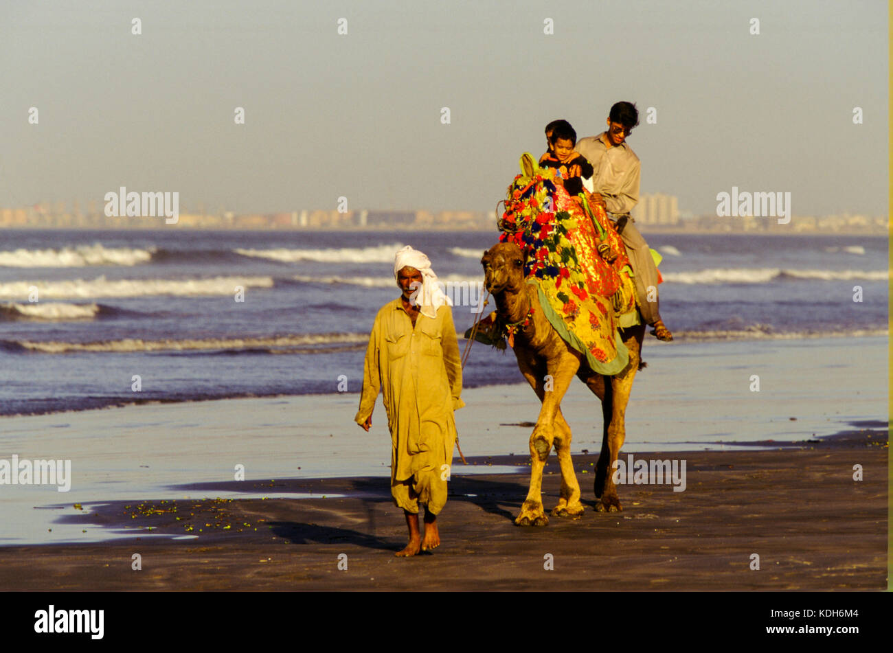 People enjoying a camel ride along the beach in Karachi, Pakistan, with ...