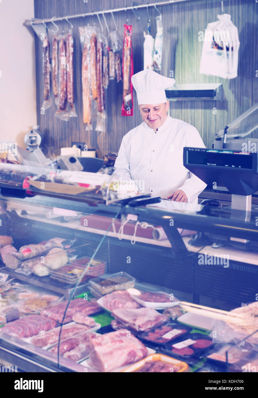 Mature male butcher with wurst and smoked meat at market counter Stock ...