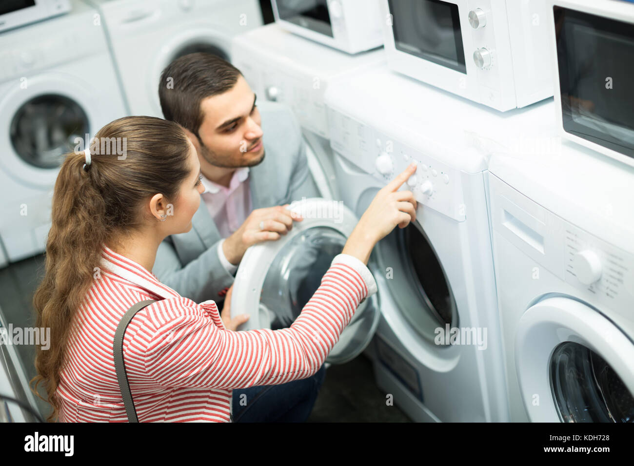 Happy young couple choosing washing machine in hypermarket and smiling ...