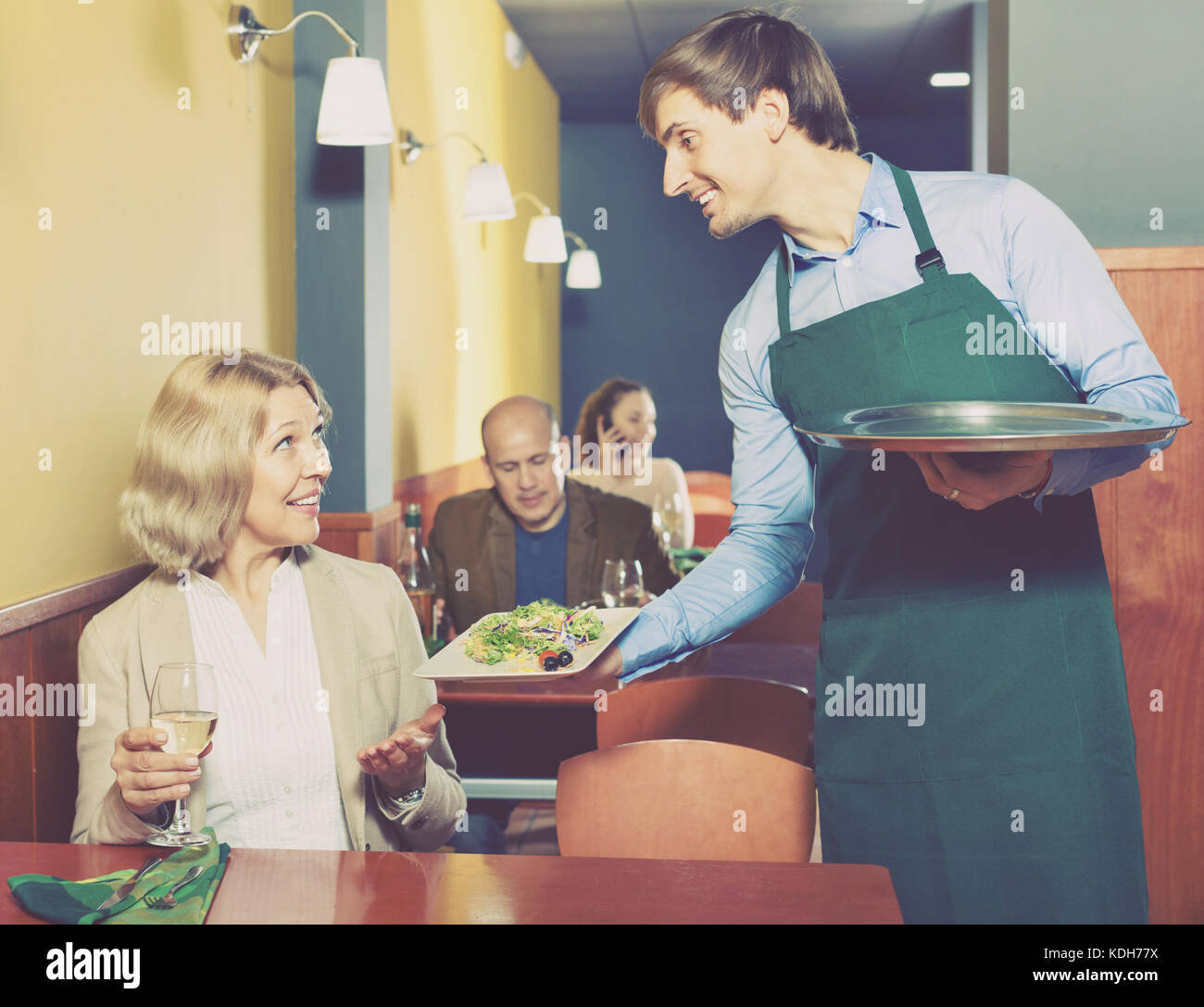Positive waiter bringing order to happy mature female in restaurant ...