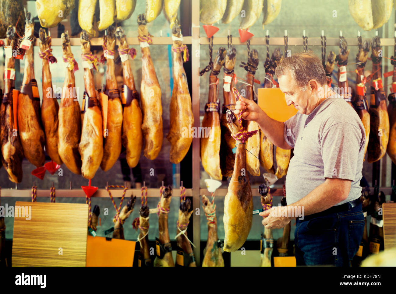 Mature man customer holding tasty jamon leg in local delicatessen store ...