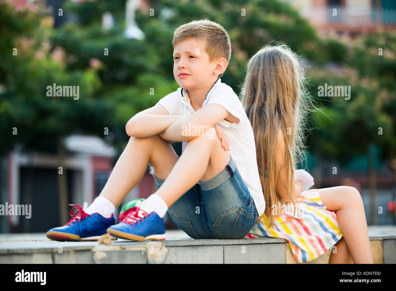 Portrait of sad little boy sitting back to friend outdoors in park ...