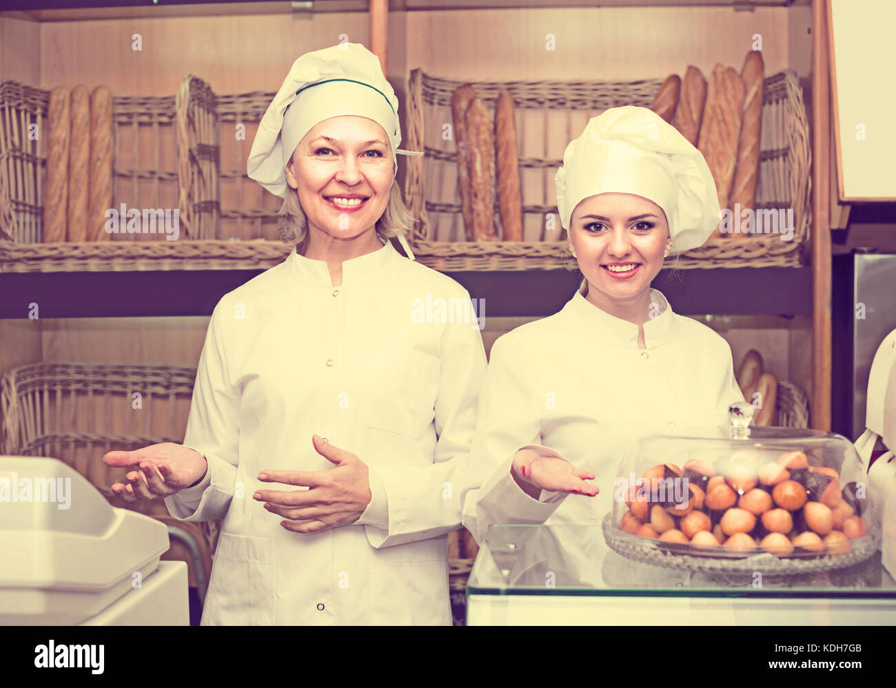 Portrait of two friendly smiling female bakers with pastry in bakery ...
