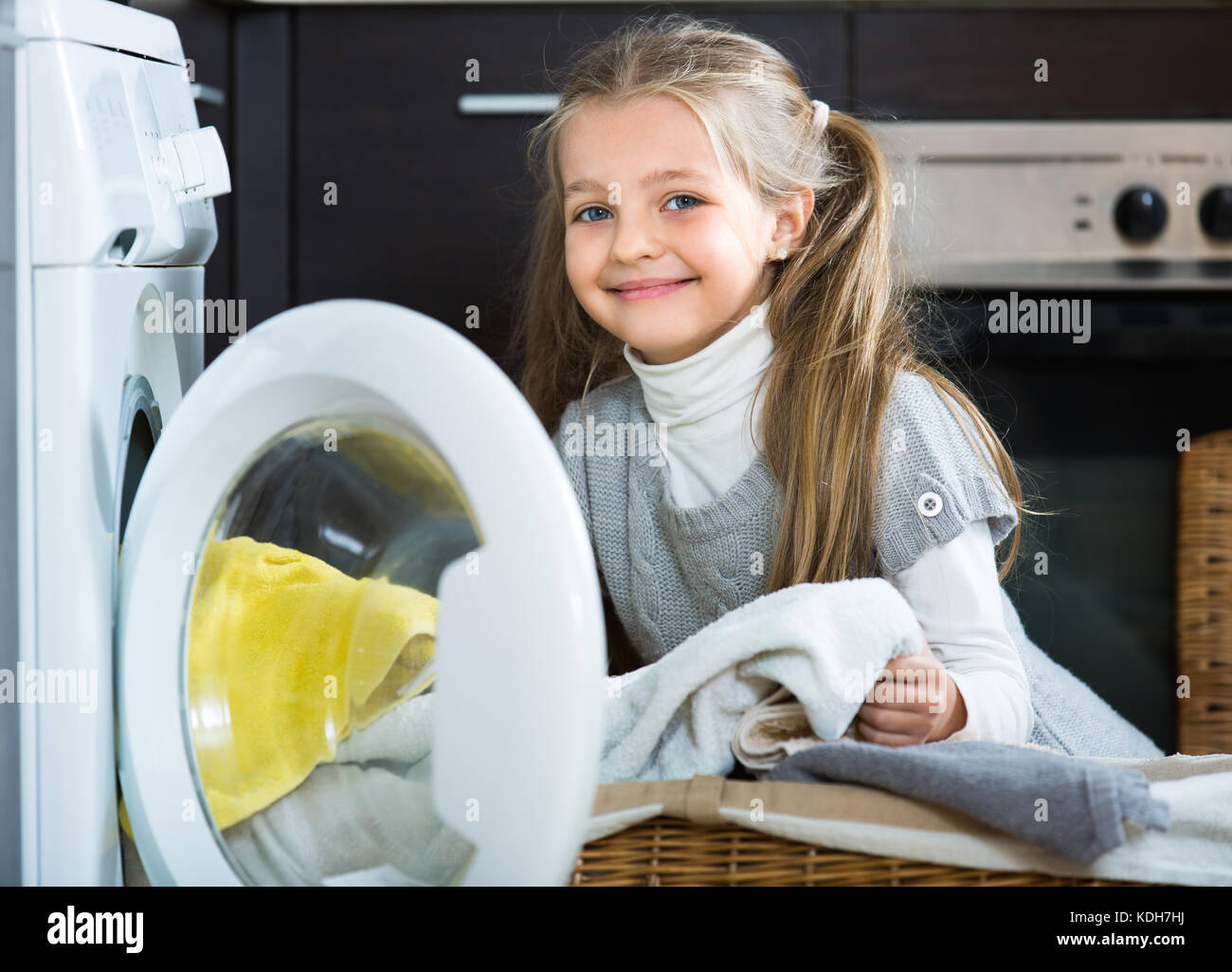 Happy smiling cute little girl with long hair doing laundry in home ...