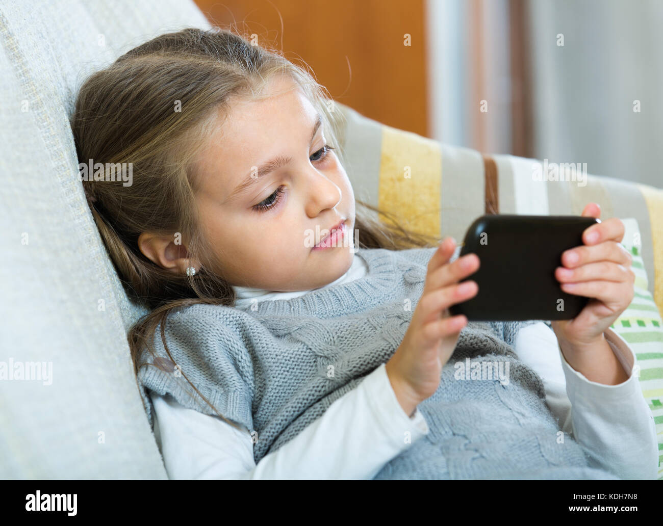 Longhaired cute little girl addicted to smartphone games at home Stock ...