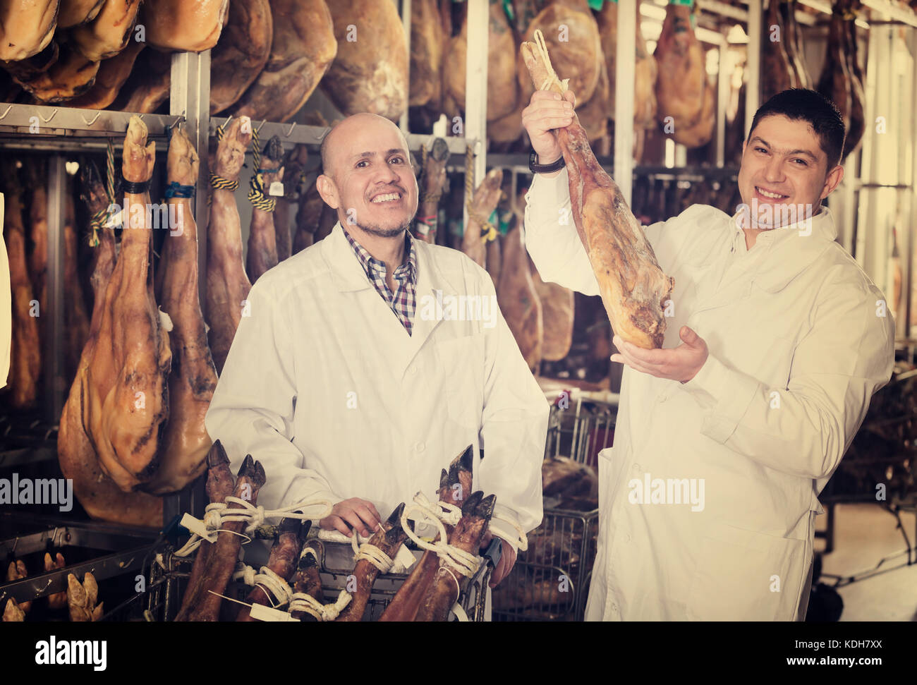 Mature butcher and his young assistant with jamon joints at the meat ...
