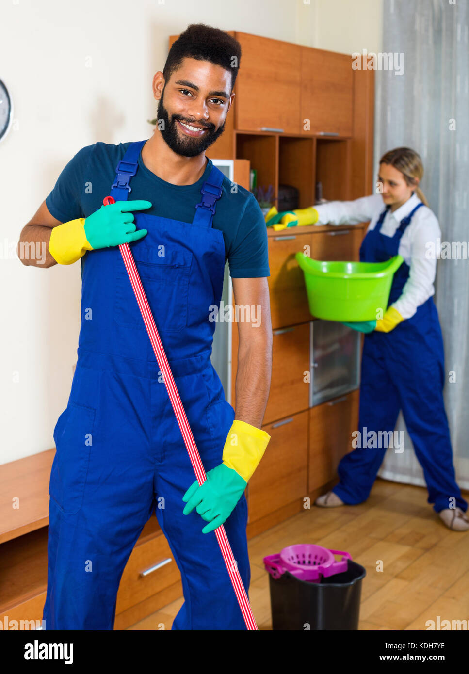 Professional smiling cleaners cleaning and dusting in ordinary house ...