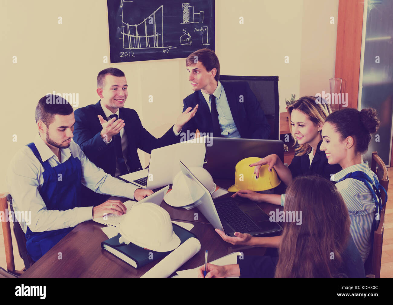 Team of young positive professionals with helmets and laptops on the ...