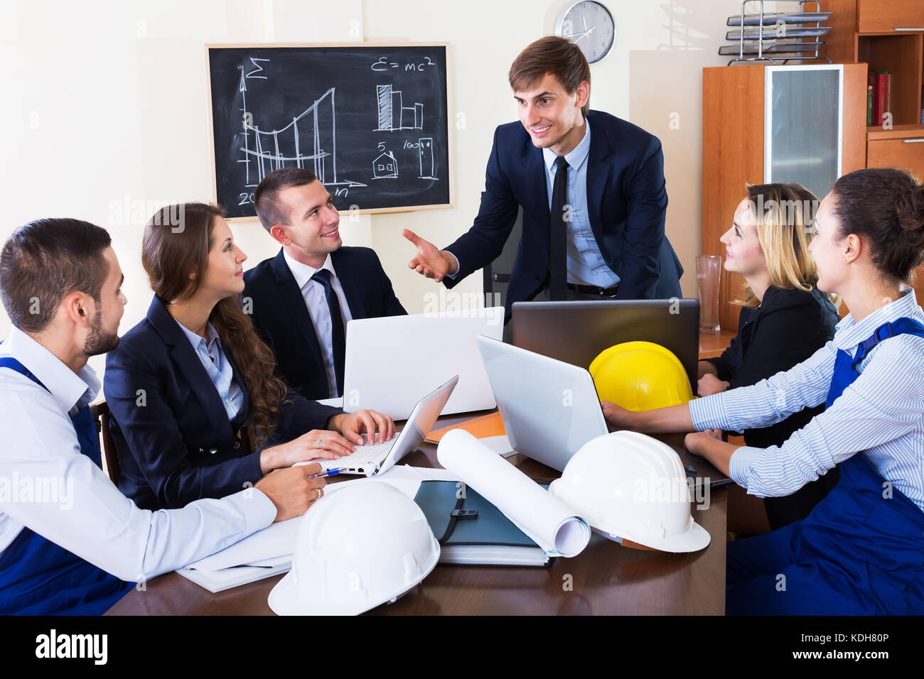 Team of young positive professionals with helmets and laptops on the ...