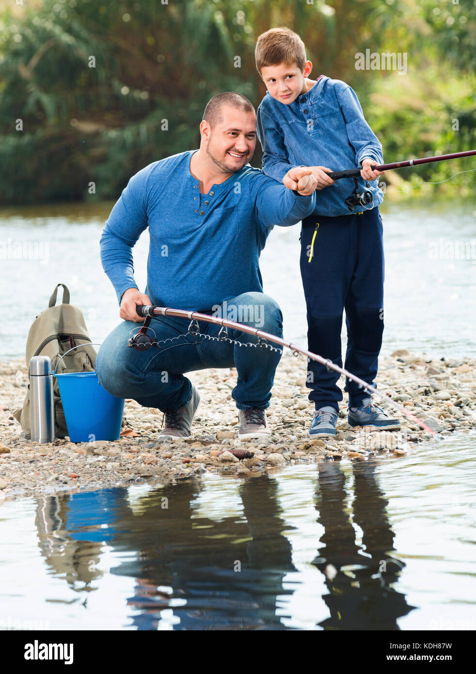 Portrait of glad smiling father and cute son fishing with rods in ...