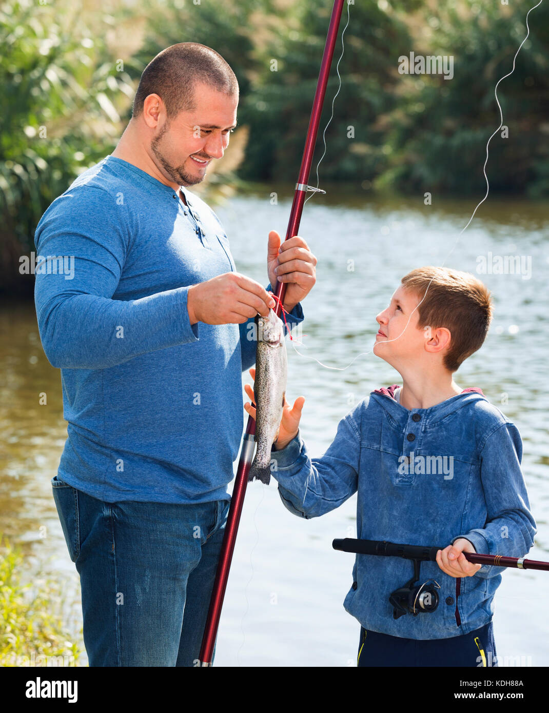 Portrait of happy friendly glad father and cute son fishing with rods ...