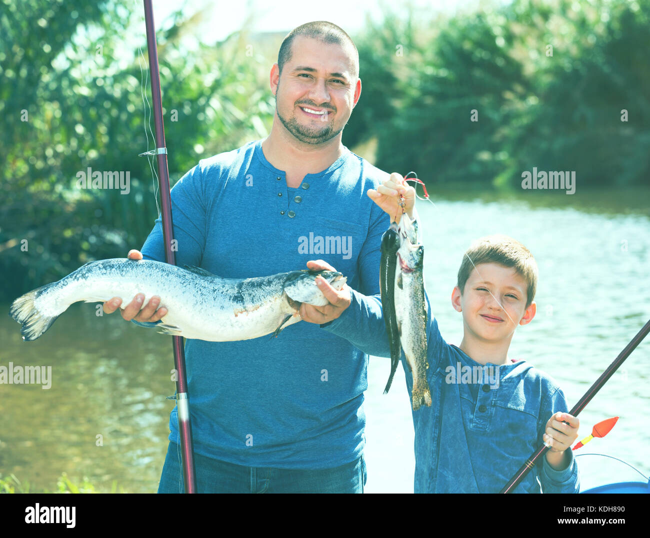 Portrait of happy friendly laughing father and son fishing with rods in ...