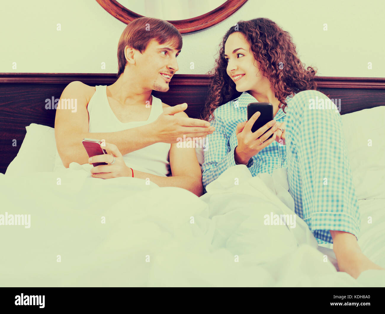 Positive boyfriend and smiling girlfriend busy with smartphones in ...