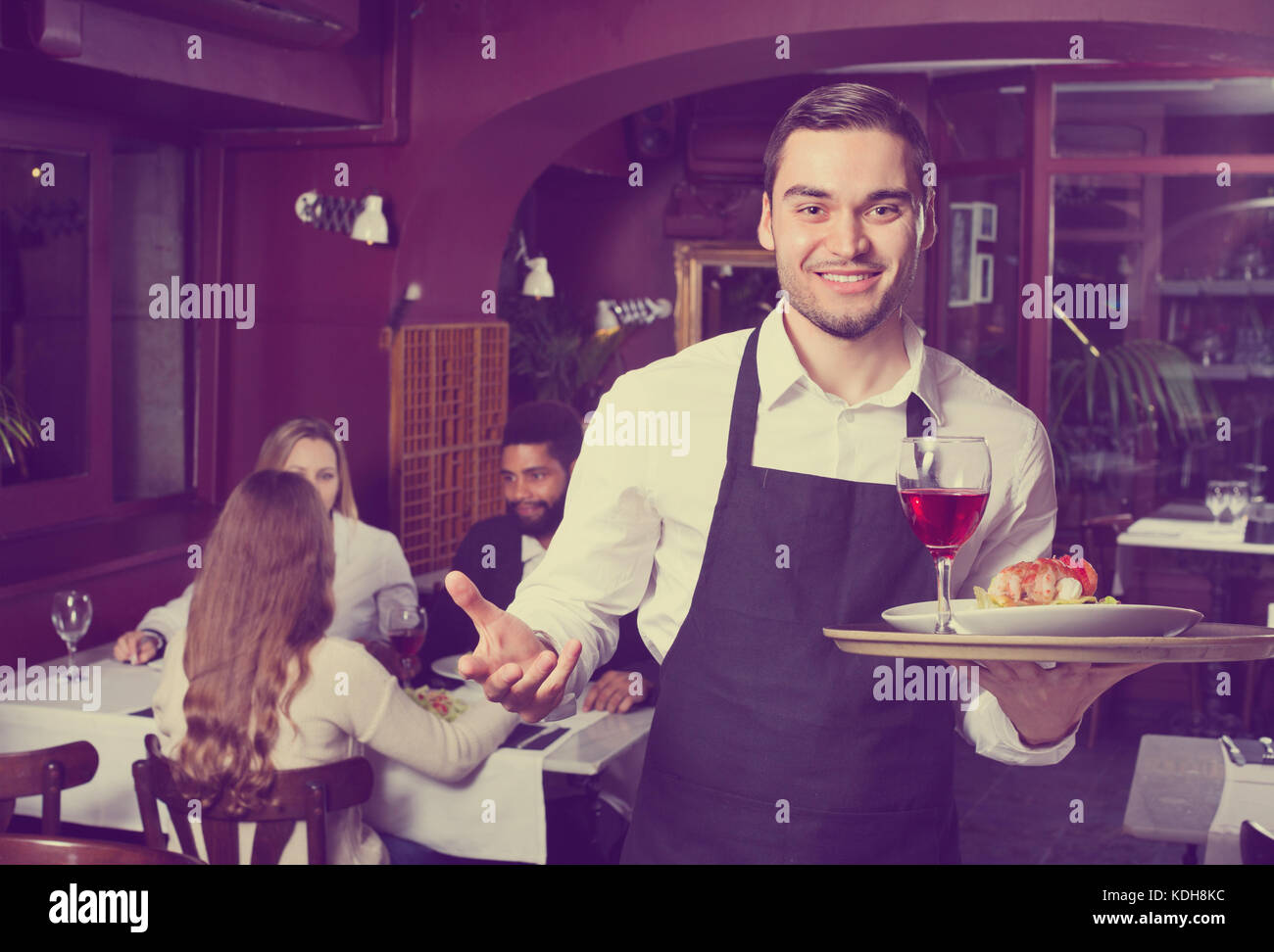 Smiling glad young waiter taking care of adults at cafe table Stock ...