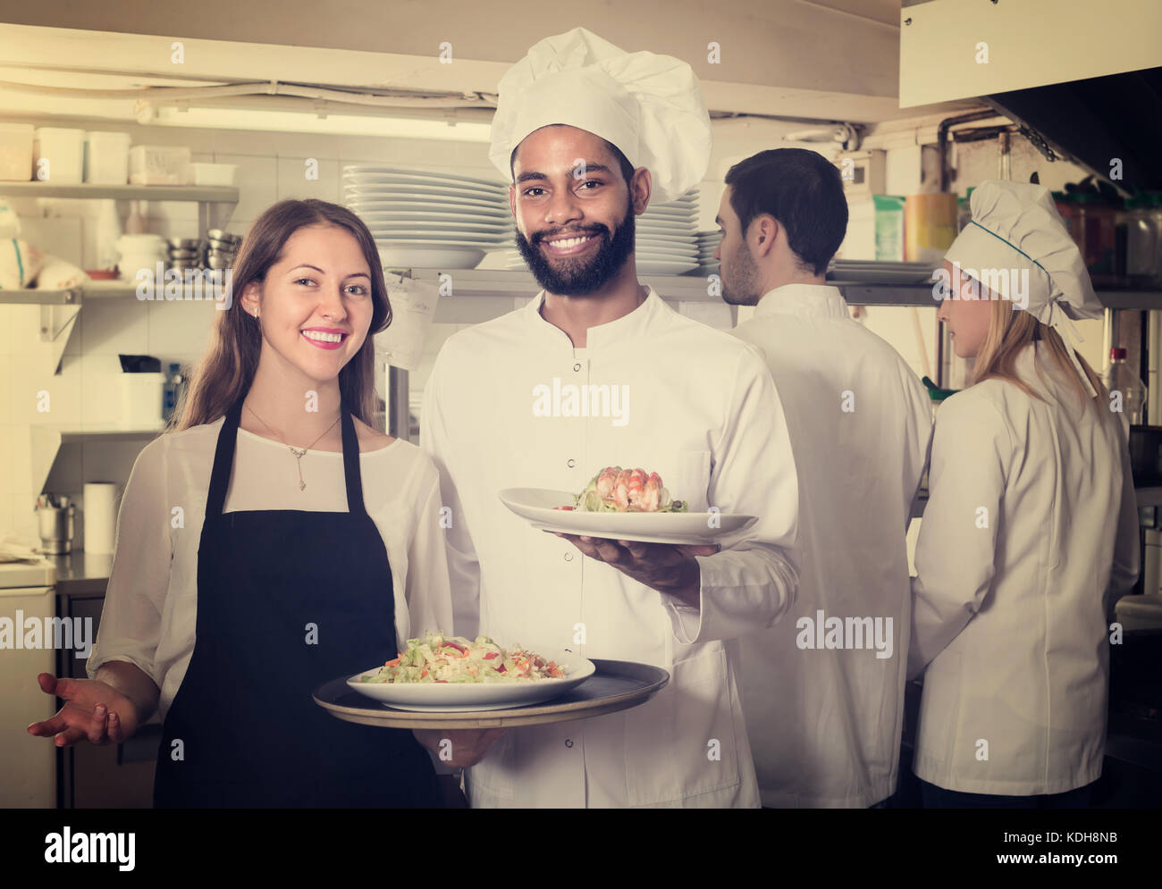 smiling waitress and crew of professional cooks posing at restaurant ...