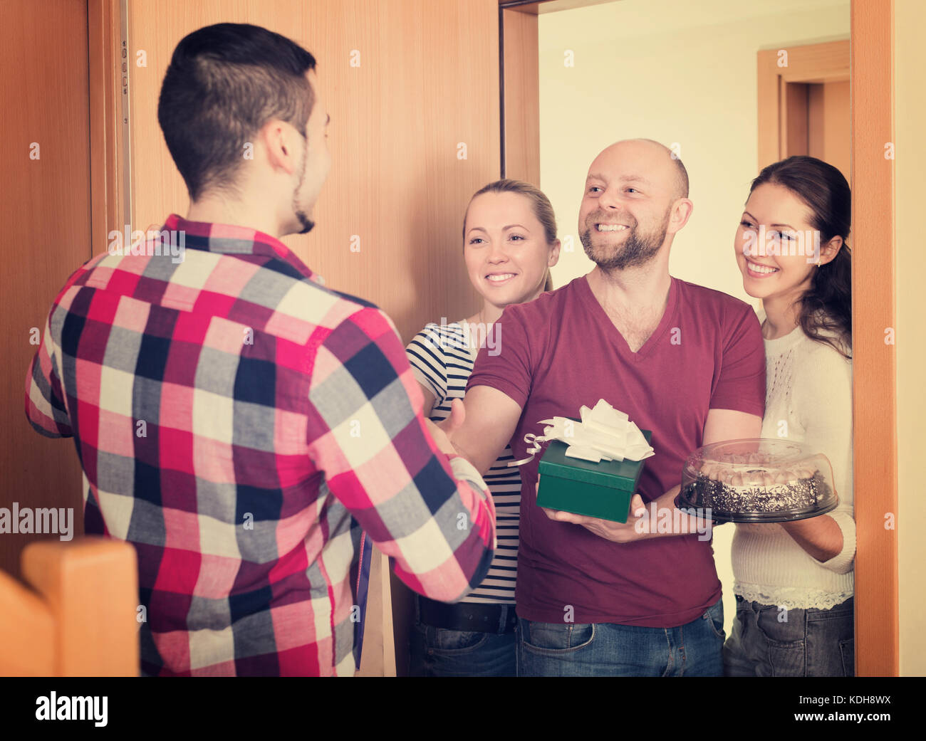 Happy smiling guests with cake and presents standing in doorway. Focus ...