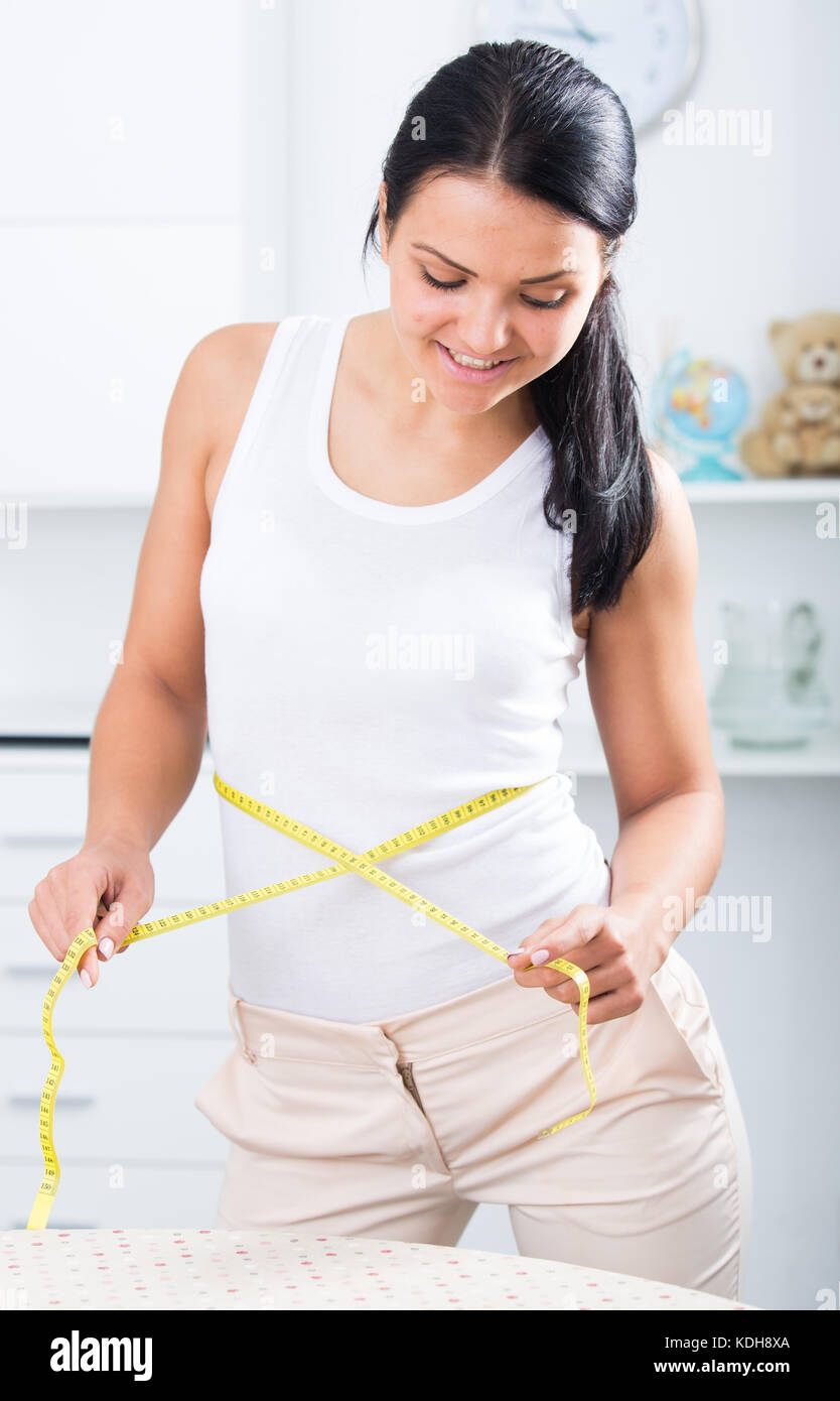 Young brunette woman measures waist by measuring tape Stock Photo - Alamy
