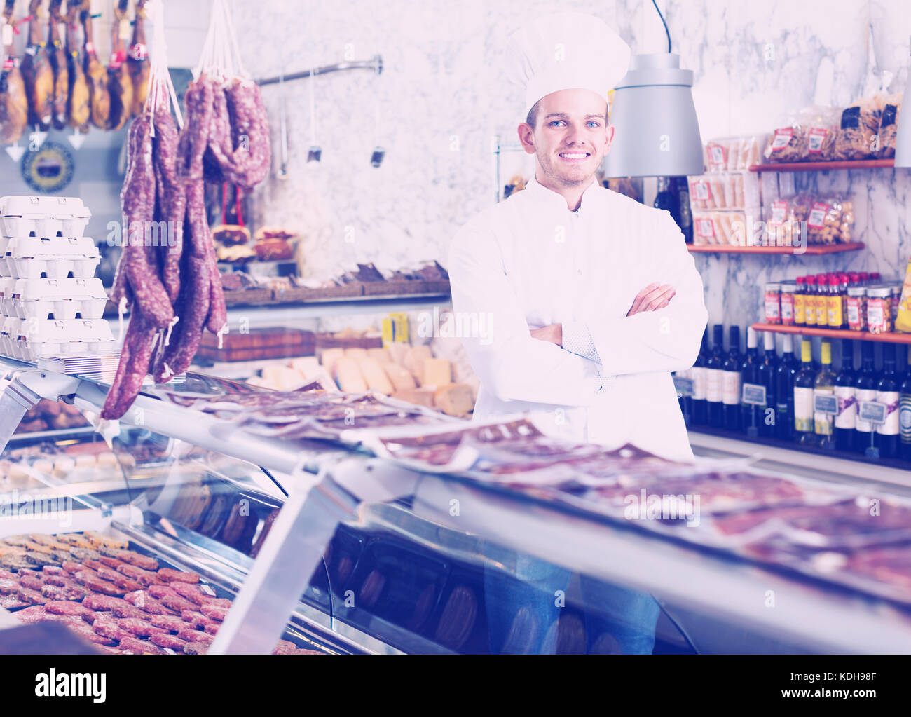 Smiling young cook in grocery shop offering meat and cheese Stock Photo ...