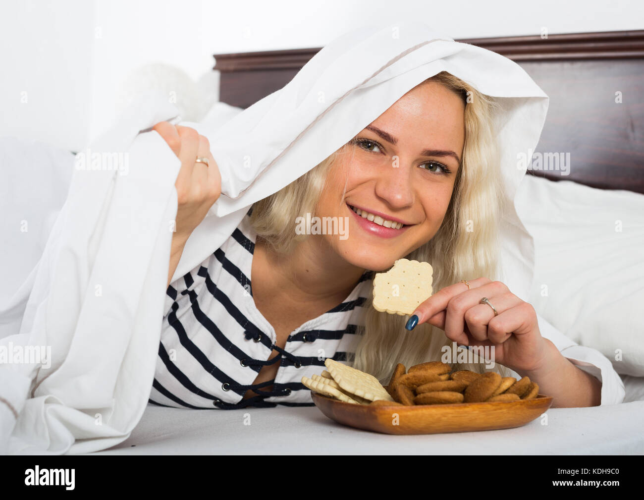 Smiling girl covered with duvet tasting sweet cooking in bed Stock ...