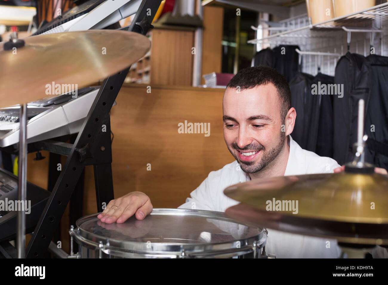 Young positive man with beard purchasing professional drum set in store ...
