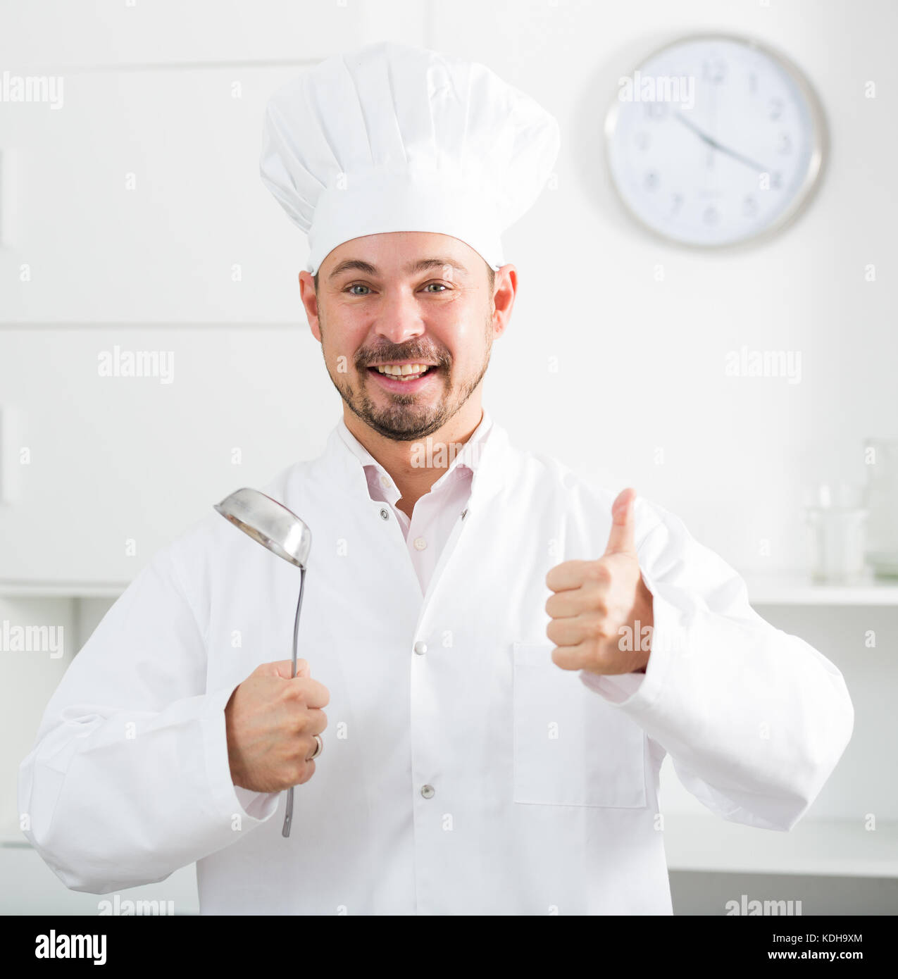 Young happy european cook in cap and with ladle smiling and gesturing ...