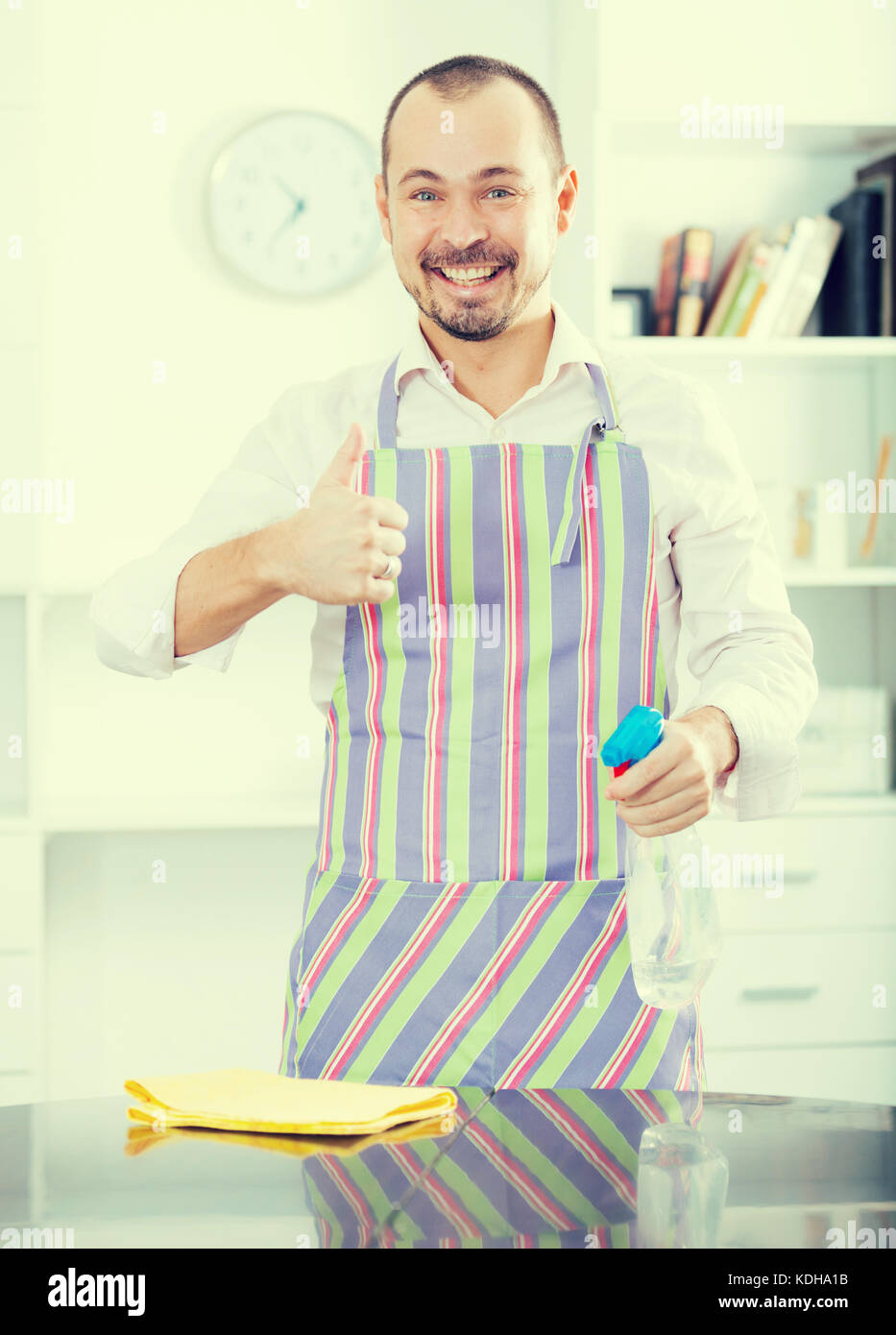 Positive young man in apron cleaning his office desk by cleanser Stock ...