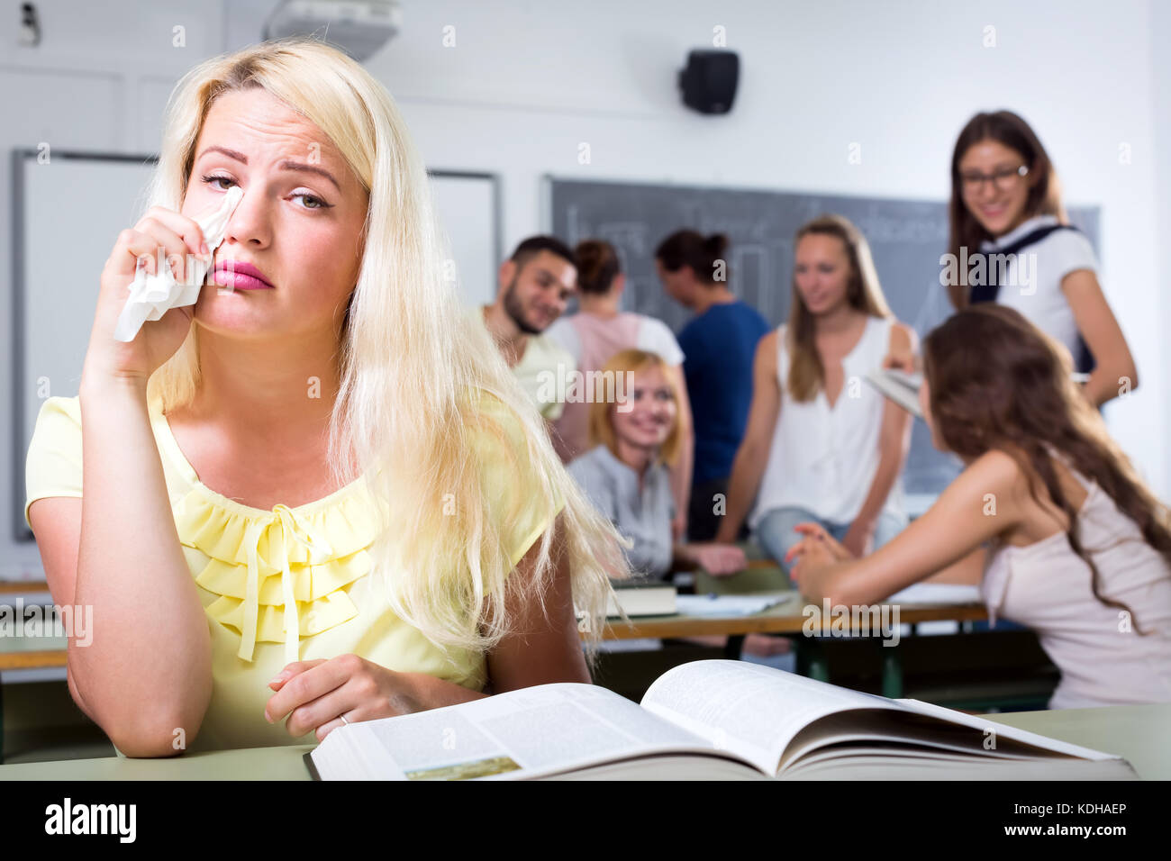 Crying female outcast student in highschool clasroom sitting at her ...
