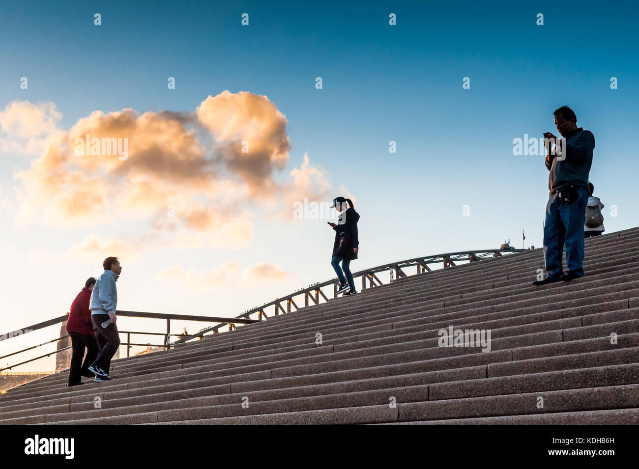 Tourists walk down the steps of The Sydney Opera House with a dramatic ...