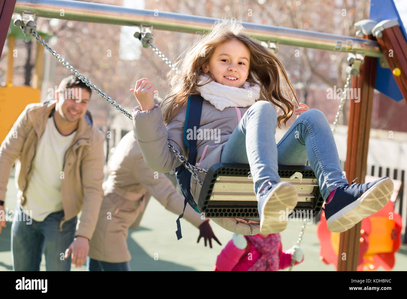 Cheerful russian family with two girls having fun on swings outdoors ...
